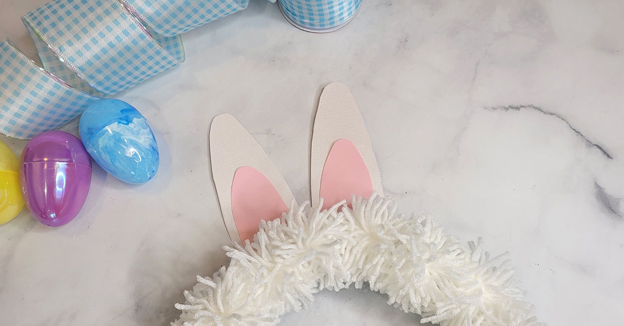 Paper bunny ears on a white pom pom wreath.