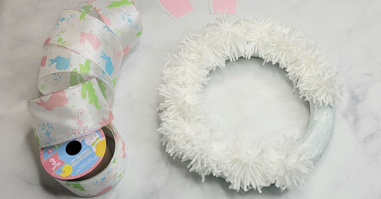 A roll of ribbon and a wreath with white pom poms on it.