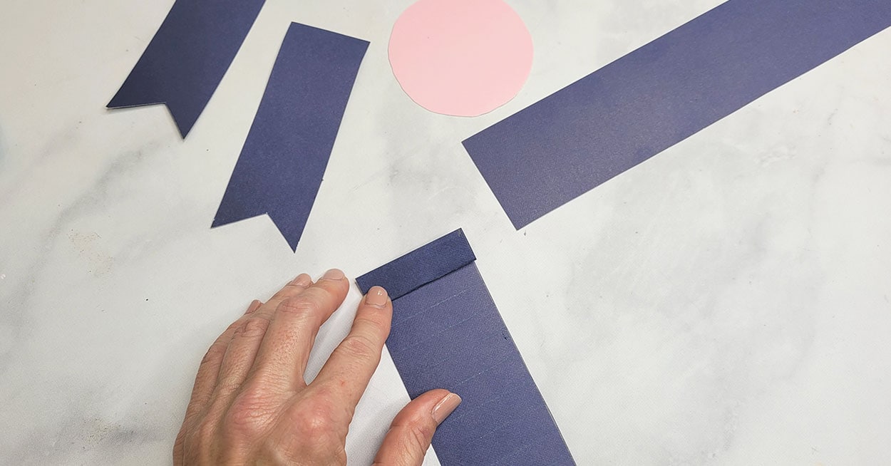 A hand folding a strip of purple paper.