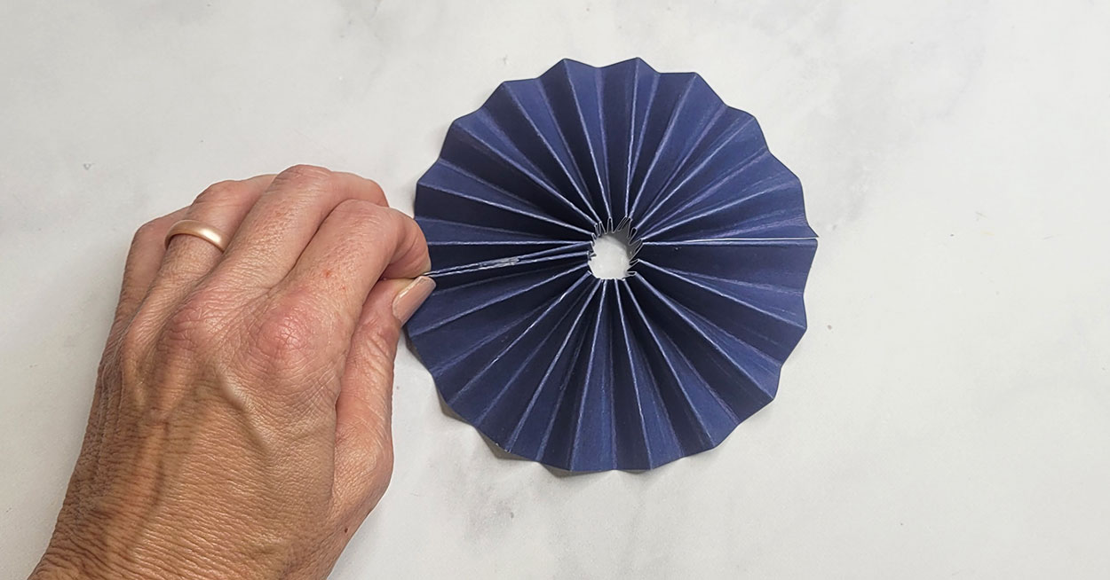 A hand holding a paper accordion circle.