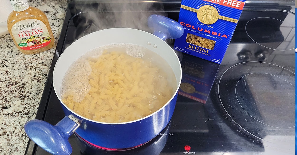 A pot of noodles boiling on a stove, a bottle of salad dressing, and a ...