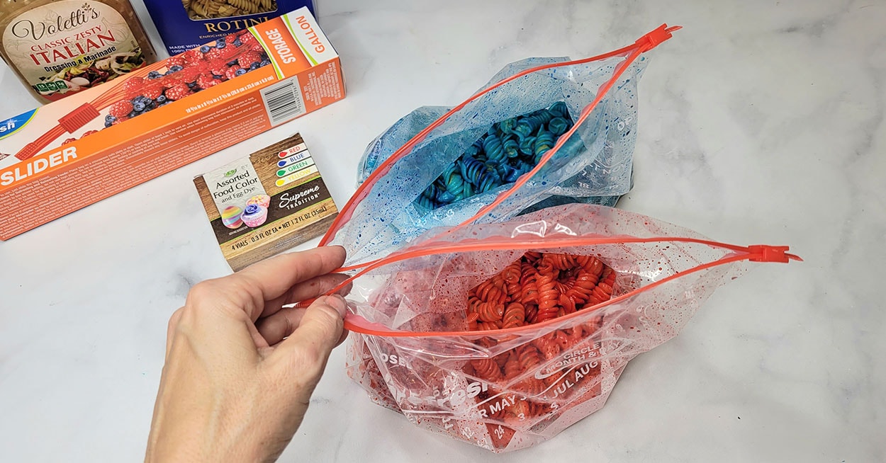 A hand holding 2 storage bags with blue and red noodles in them, a box ...