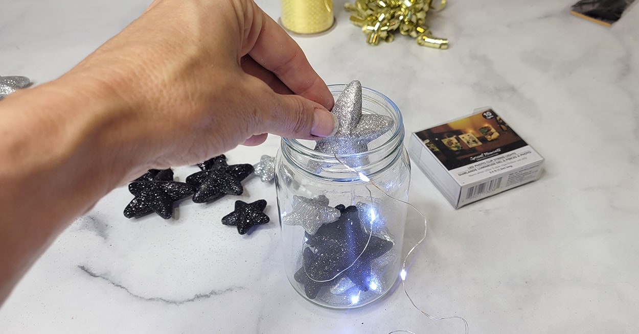 A hand putting a glitter star in a jar with black stars and lights in it.