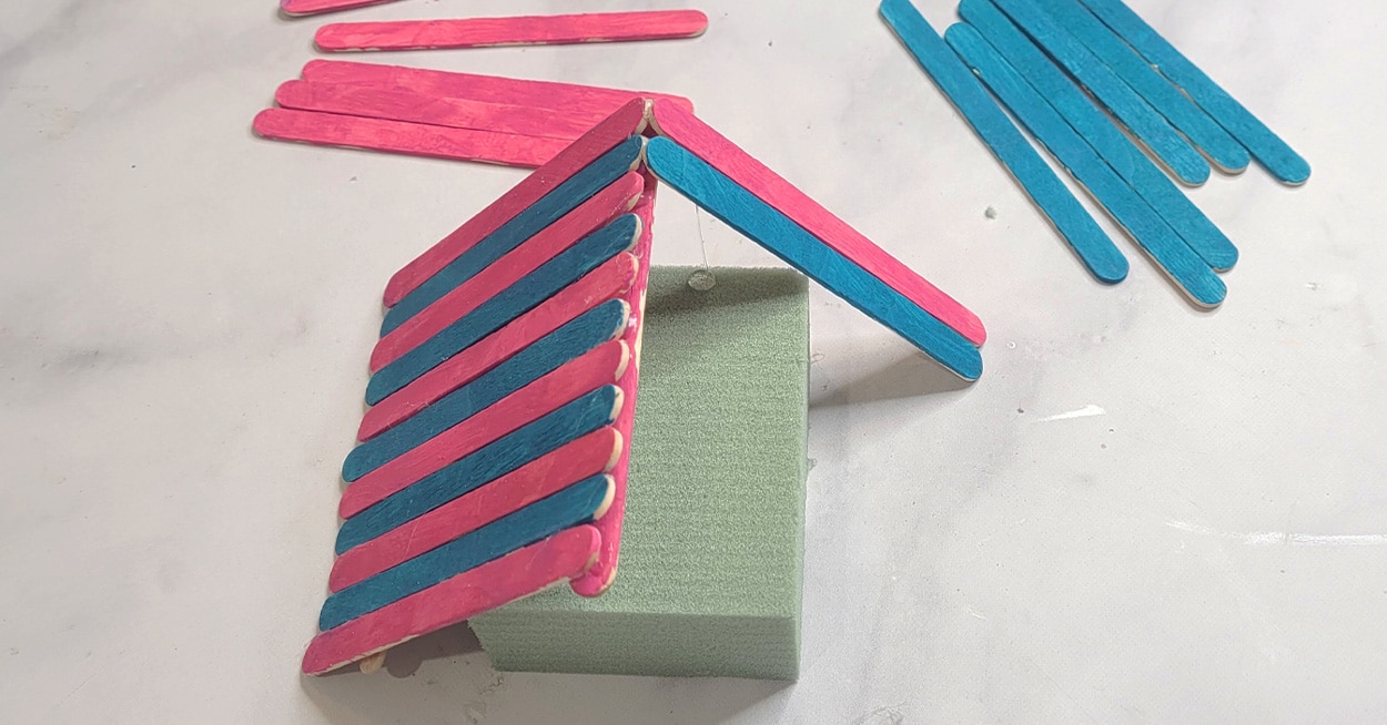 A piece of floral foam with pink and blue craft sticks on it and more ...