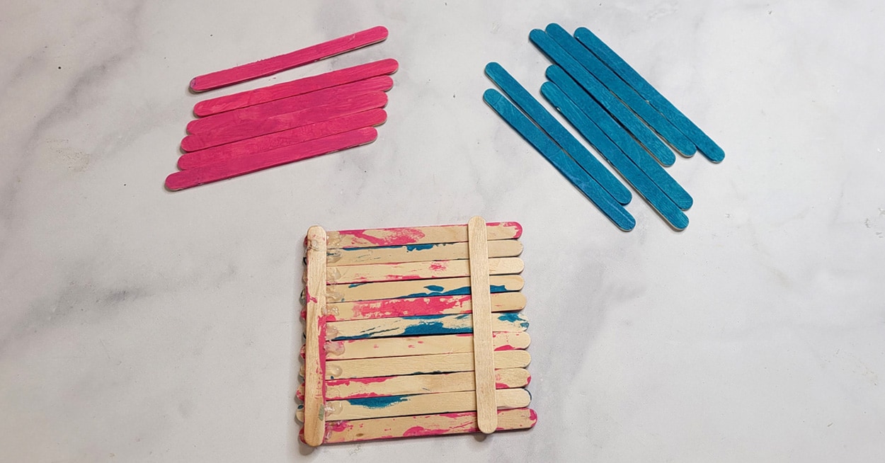 A piece of floral foam with pink and blue craft sticks on it and more ...