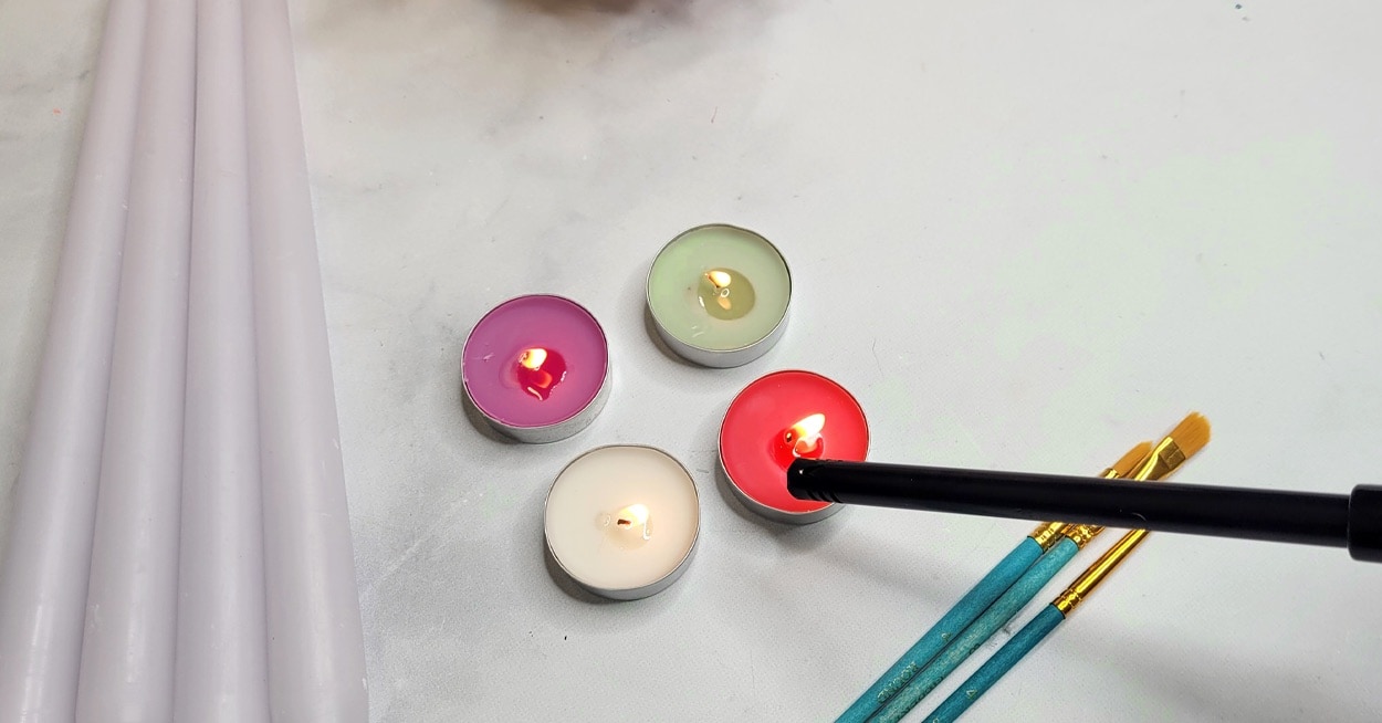 A lighter lighting some tea light candles, 4 white taper candles, and 3 ...